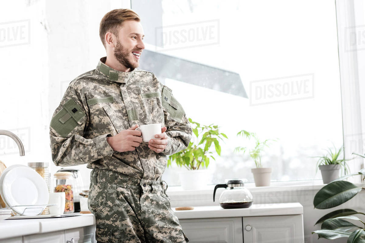 smiling army soldier holding cup of coffee in kitchen - Royalty-free ...