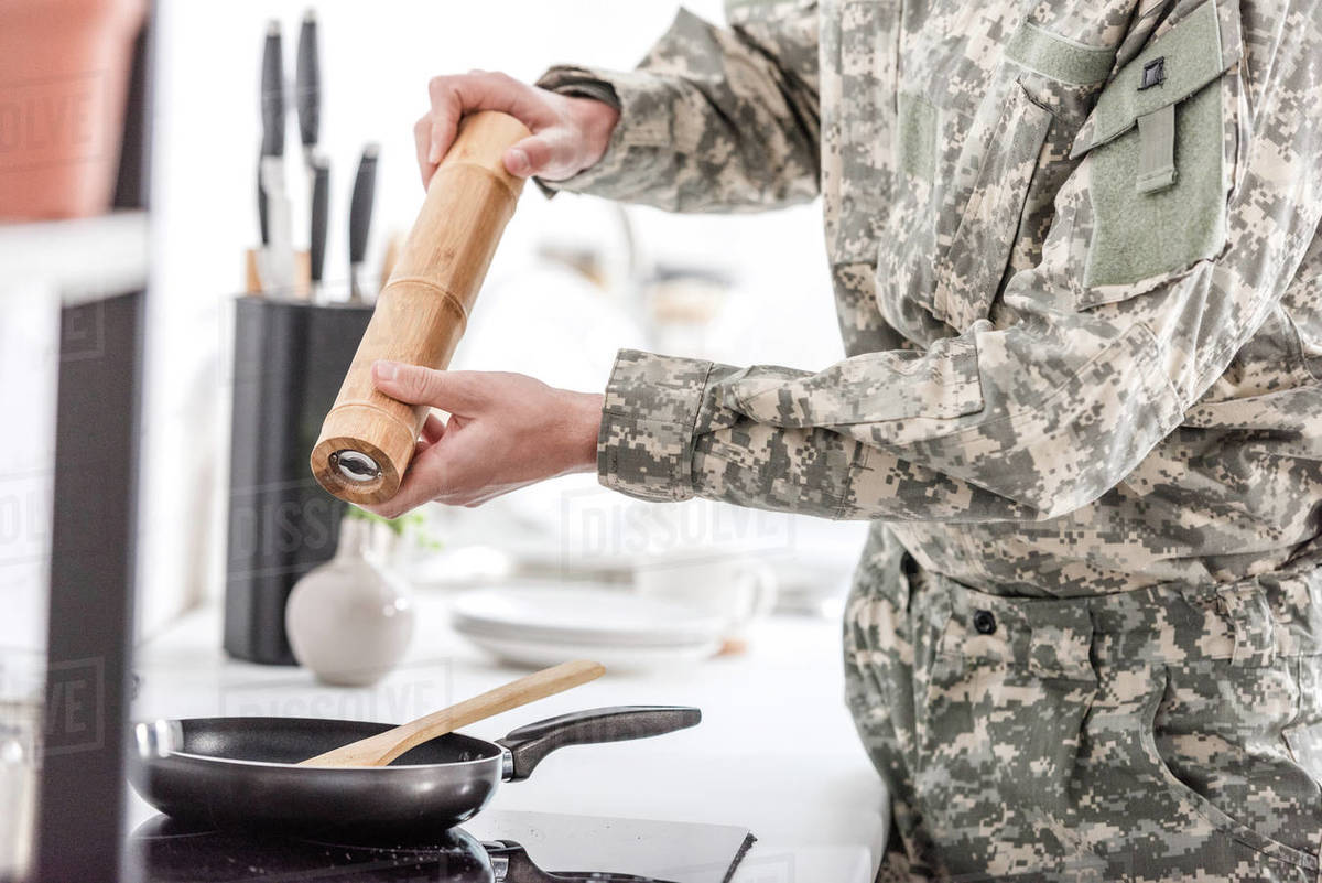 cropped view of army soldier using pepper pot while cooking in kitchen ...