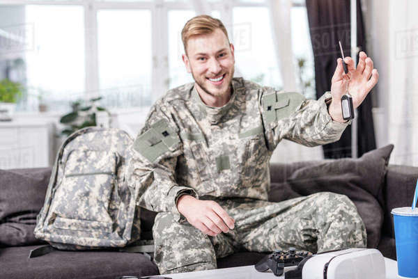excited army soldier sitting on couch at home, looking at camera and ...