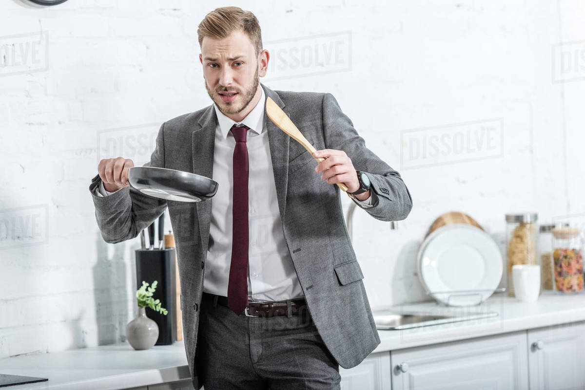 confused businessman in formal wear holding spatula with pan and ...