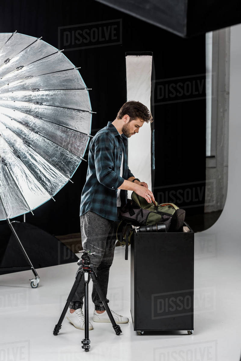 Side view of professional young photographer packing camera in backpack ...