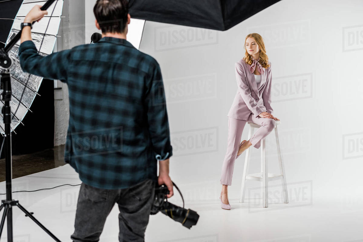 Back view of photographer holding camera and model posing in studio ...