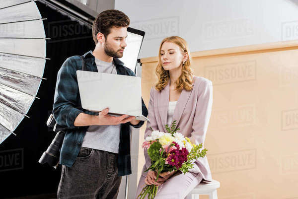 Low angle view of photographer showing laptop to beautiful young model ...