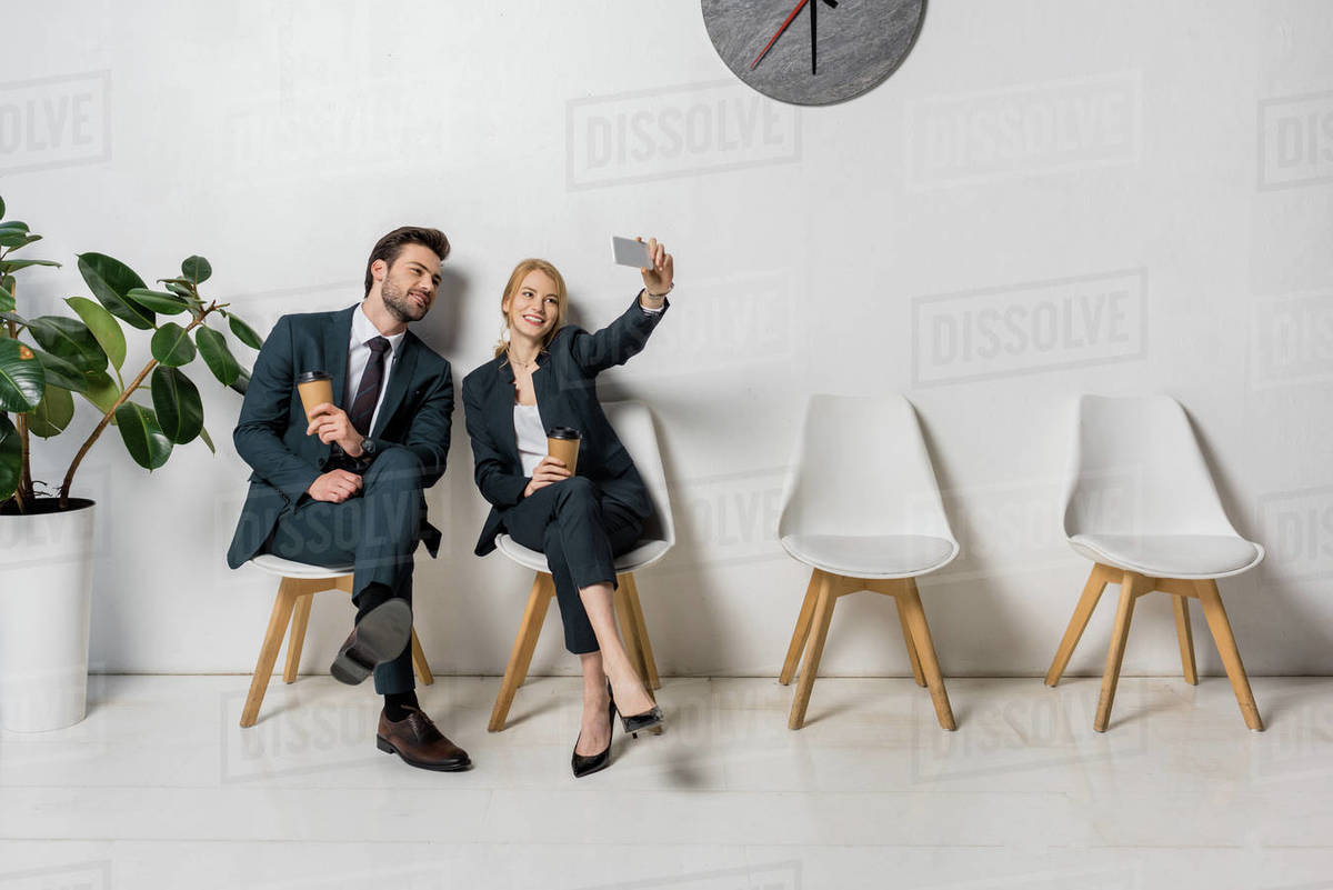 Smiling business people taking selfie with smartphone while sitting on ...