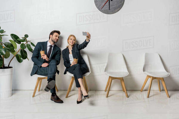 Smiling business people taking selfie with smartphone while sitting on ...