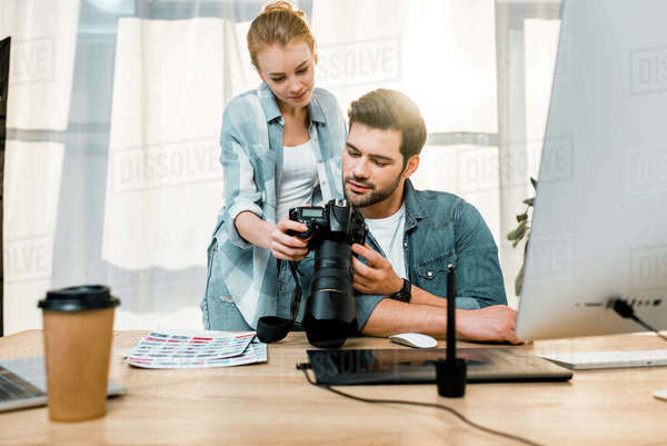 Professional smiling young photographers using photo camera together in ...
