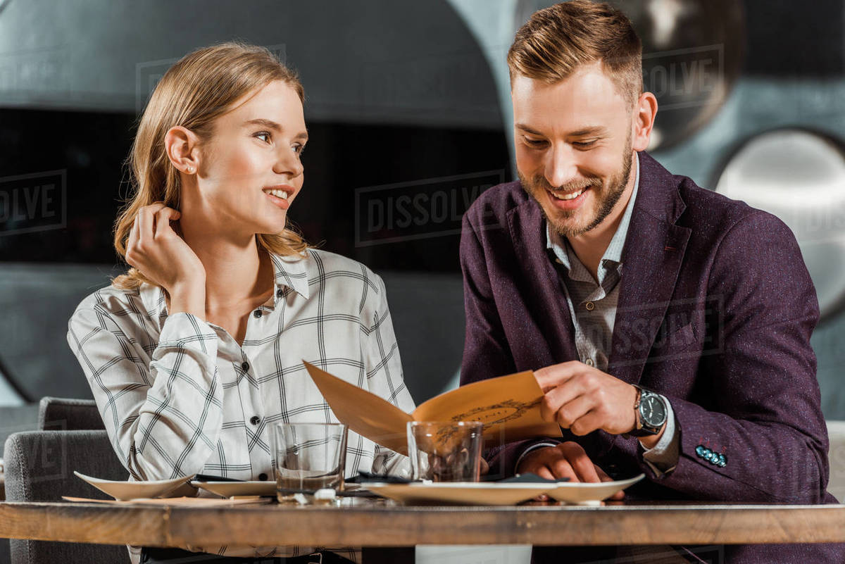 Happy smiling couple looking in menu to order dinner in restaurant ...