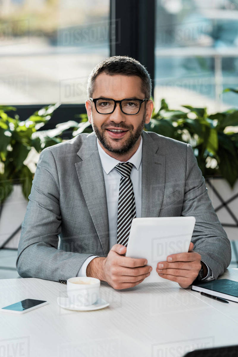 Cheerful handsome businessman holding tablet and looking at camera in ...