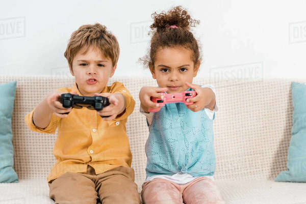 Adorable multiethnic kids playing video game with joysticks and looking ...
