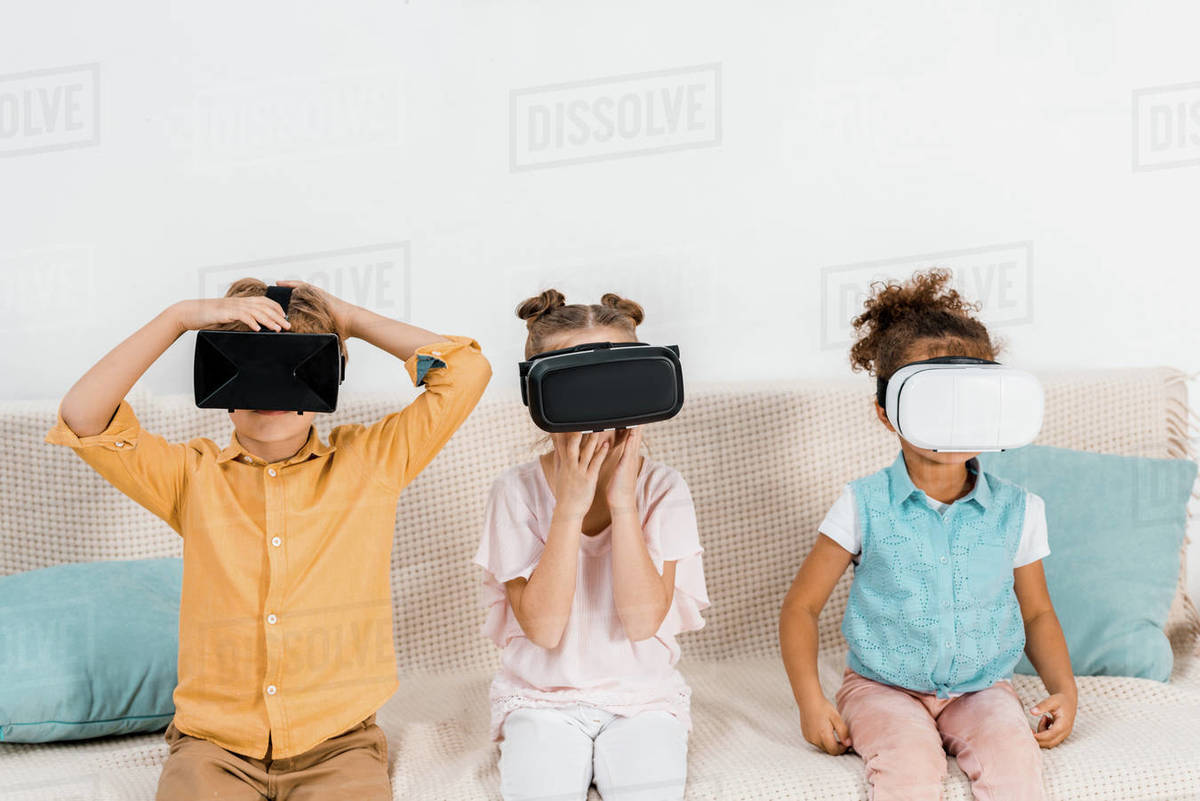 Adorable multiethnic children sitting in sofa and using virtual reality ...