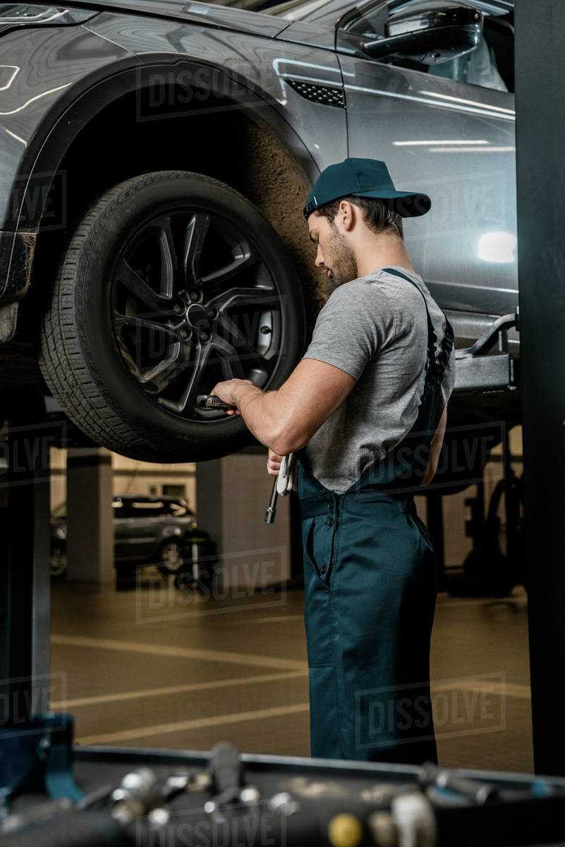 Auto mechanic in uniform fixing car wheel at auto repair shop - Royalty ...