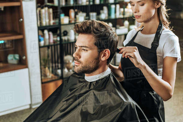 cropped shot of hairdresser combing hair to handsome young man in ...