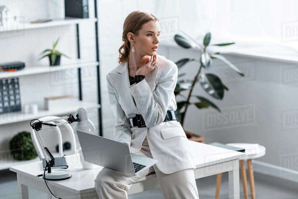 Beautiful businesswoman in white formal wear sitting on desk with ...
