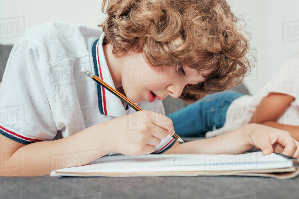 Adorable curly little boy doing homework - Stock Photo - Dissolve