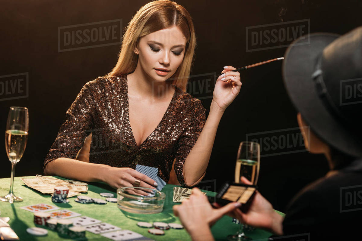 Attractive girls smoking cigarettes and playing poker at table in ...