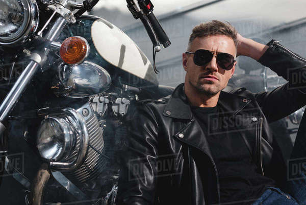 Handsome guy in sunglasses sitting by motorcycle in garage - Royalty ...