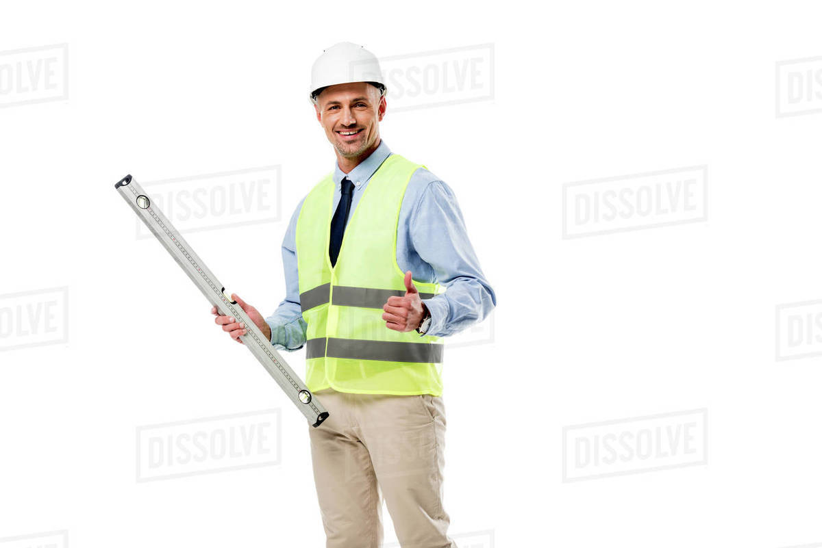 Smiling engineer holding spirit level and showing thumb up isolated on ...