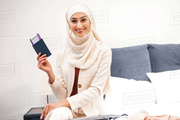 Happy young muslim woman holding passport with boarding pass and ...