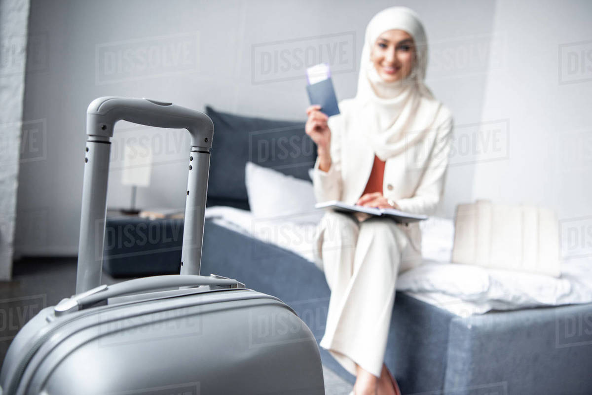 Close up View Of Suitcase And Smiling Muslim Woman Holding Passport With Boarding Pass At Home 