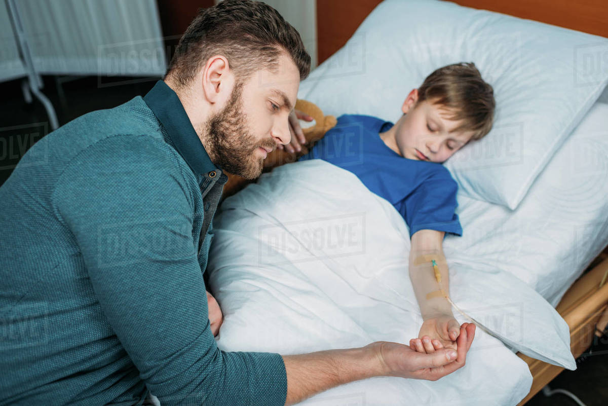 Portrait of pensive dad sitting near sick son in hospital bed - Royalty ...