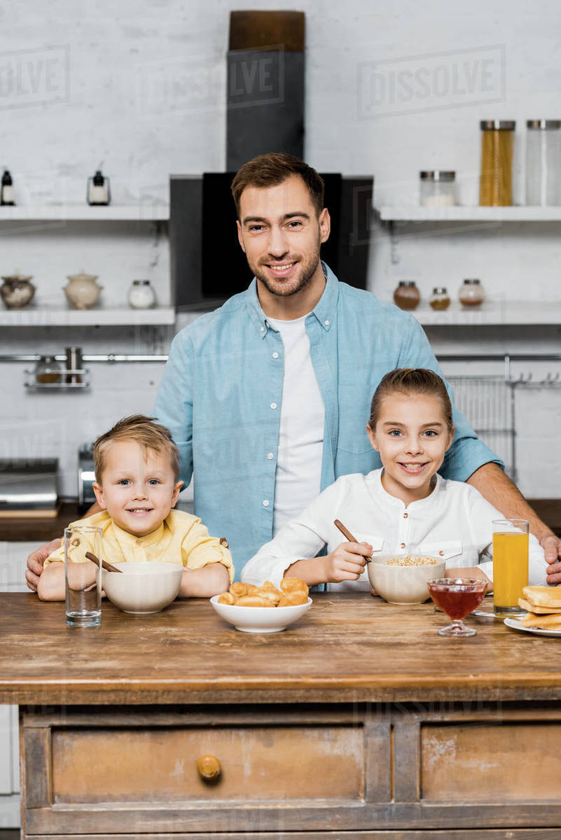 Smiling father with siblings looking at camera at kitchen table ...