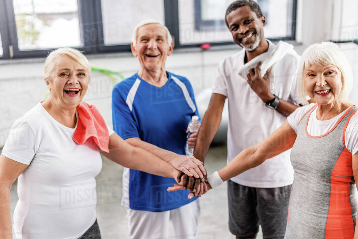 Laughing senior multicultural sportspeople putting hands together at ...