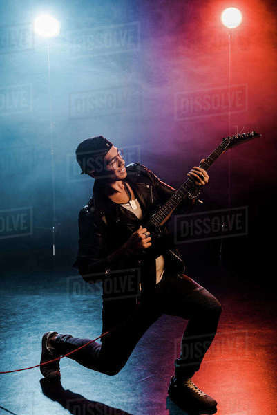 Smiling male rock star in leather jacket performing on electric guitar ...