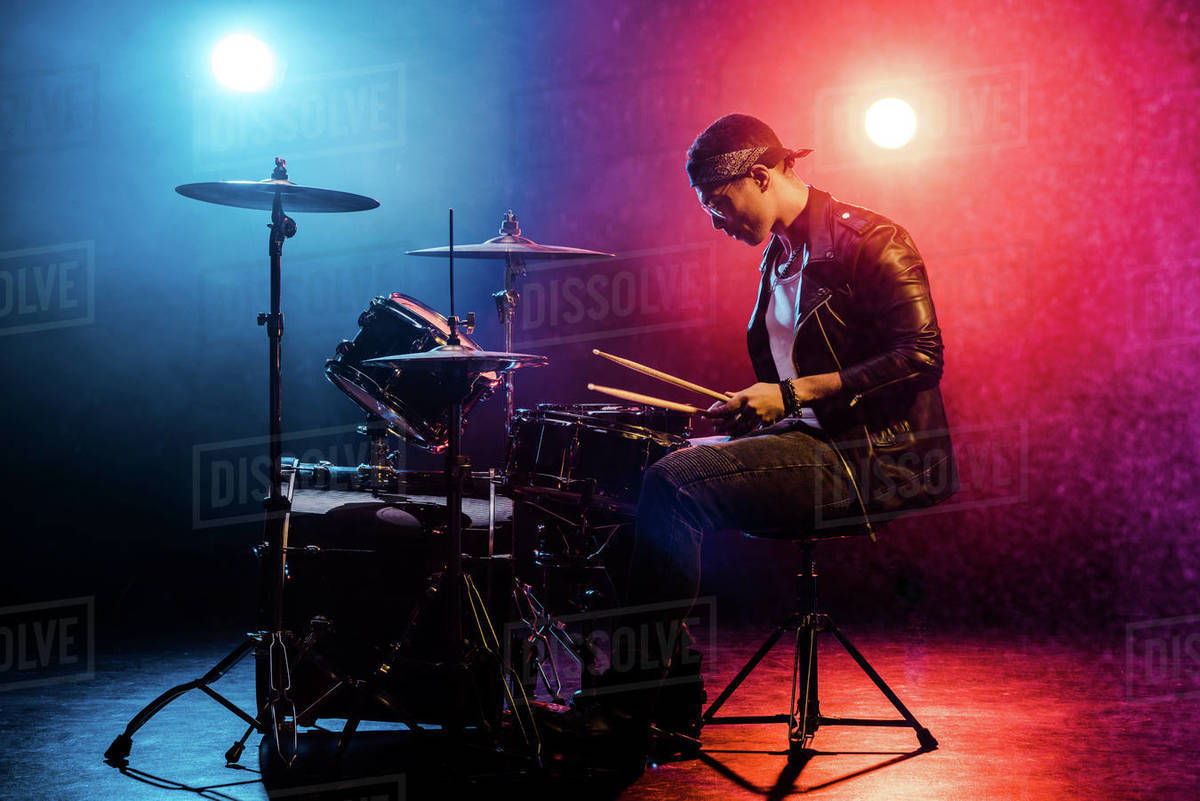 Side view of male musician in leather jacket playing drums during rock ...