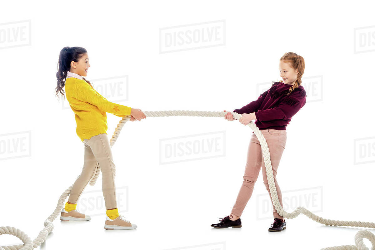 Two cheerful schoolgirls pulling rope and looking at each other ...