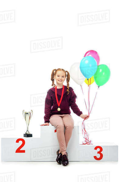 Smiling schoolgirl sitting on winner podium near trophy cup, holding ...