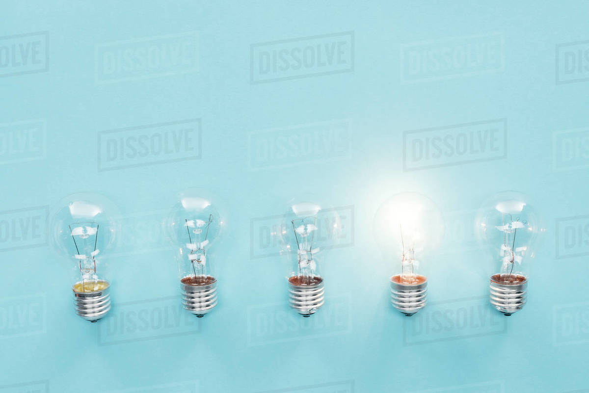 Top view of light bulbs in row and one of them glowing on blue ...