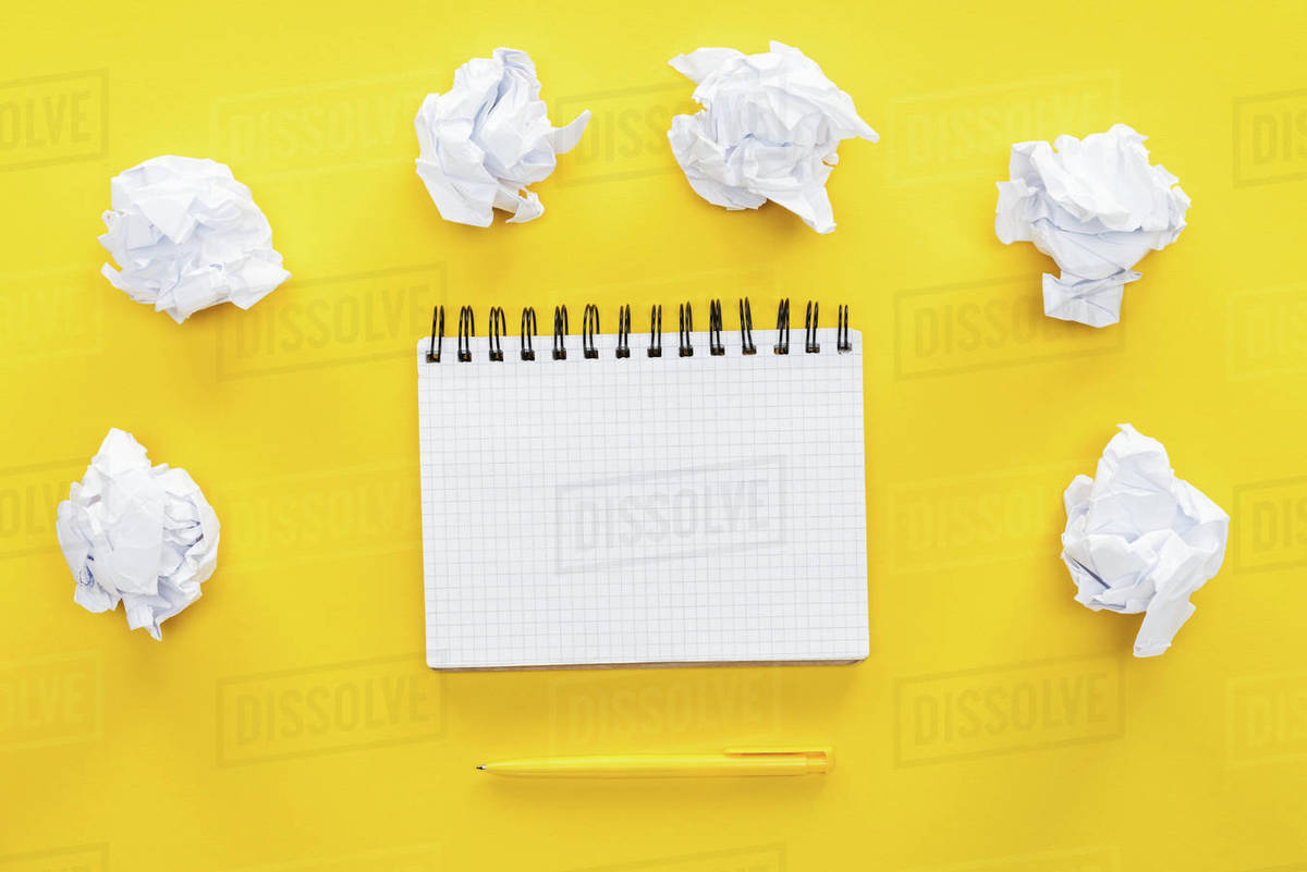 Blank spiral notebook and crumbled paper balls on yellow background ...
