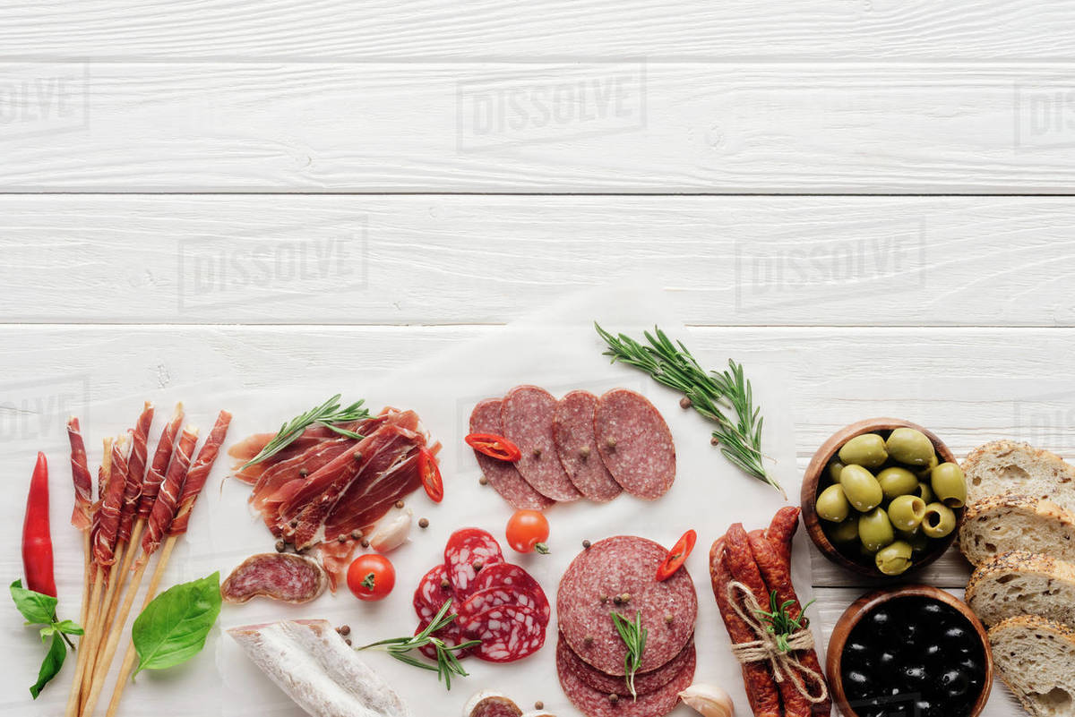 Top view of arrangement of various meat snacks and olives on white ...