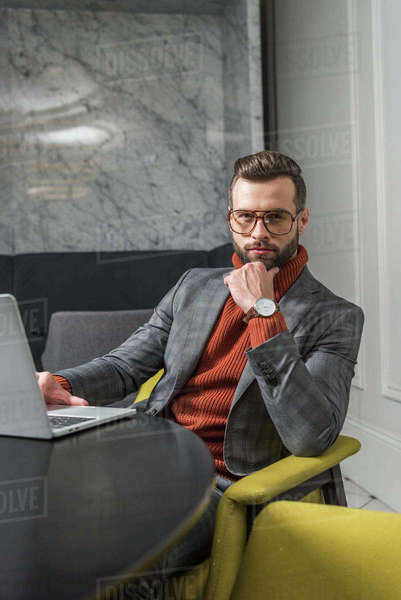Thoughtful handsome businessman sitting at table and using laptop in ...