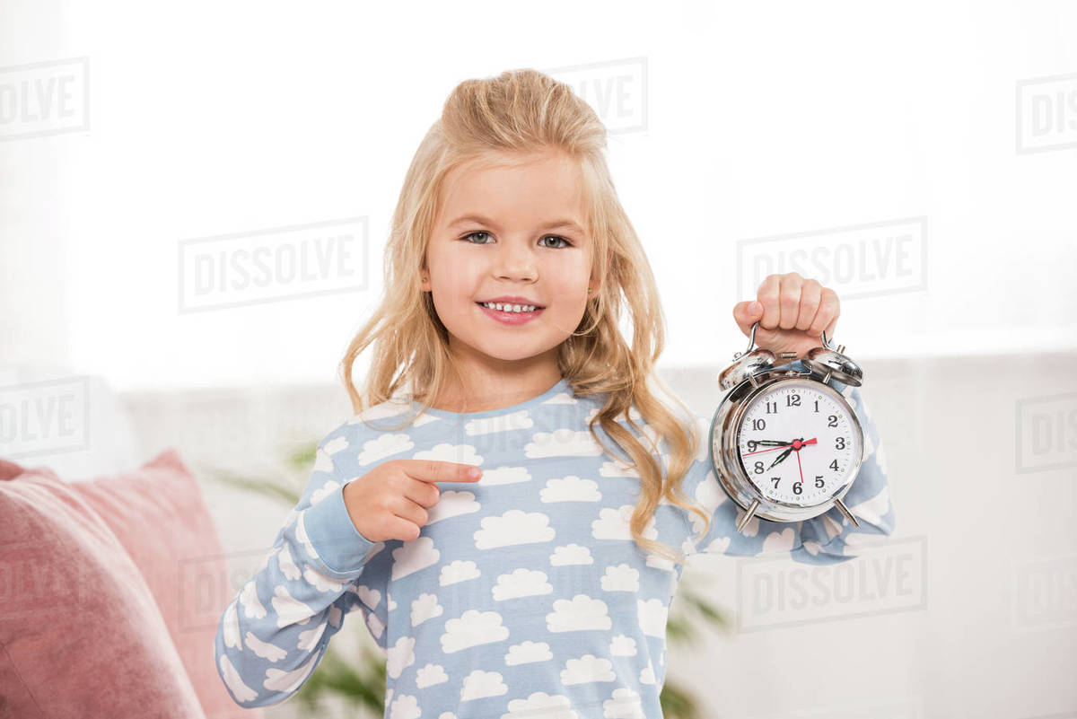 Smiling cute child pointing with finger at clock - Stock Photo - Dissolve