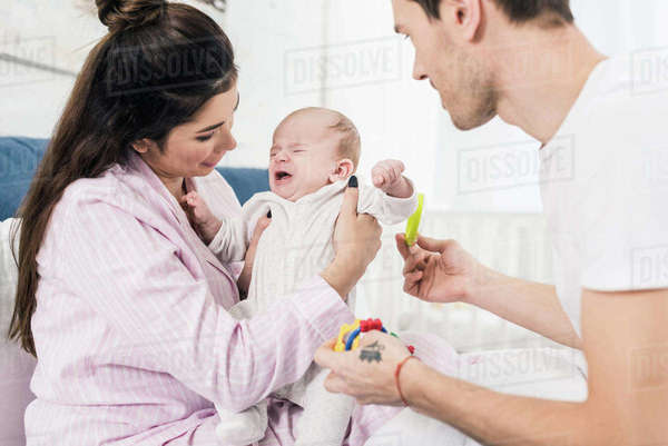 Mother holding crying baby in hands with father near by at home ...