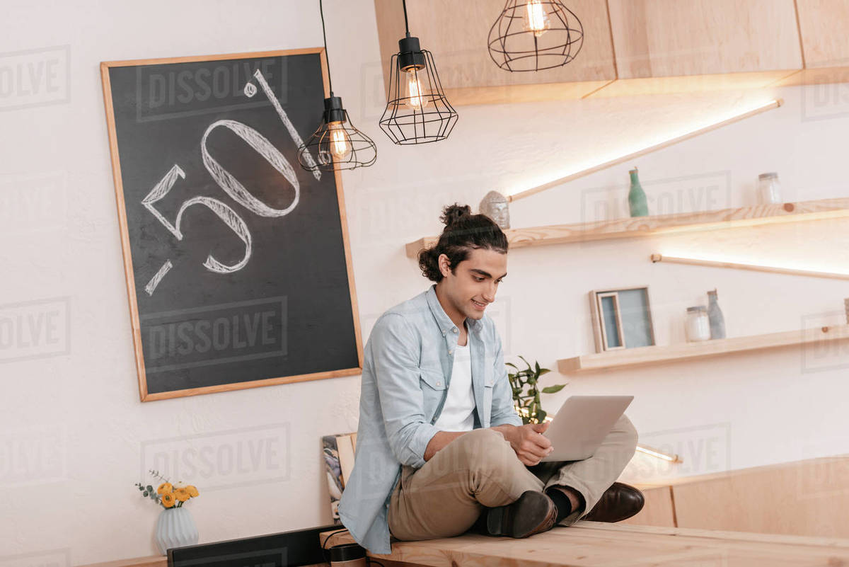 Handsome smiling young man using laptop while sitting and working in ...