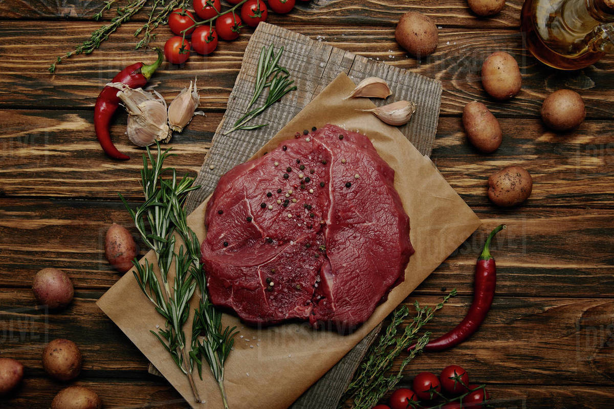 Flat lay with raw meat on baking paper with vegetables and rosemary on ...
