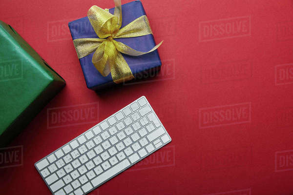 Cropped view of wrapped gifts near white computer keyboard on red ...