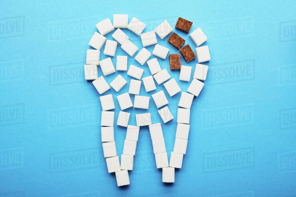 Top view of white and brown sugar cubes arranged in tooth sign on blue ...