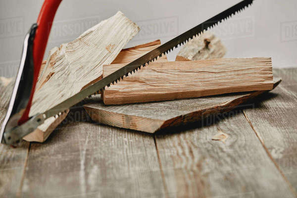 Close up view of hacksaw and wood logs on wooden table on grey ...