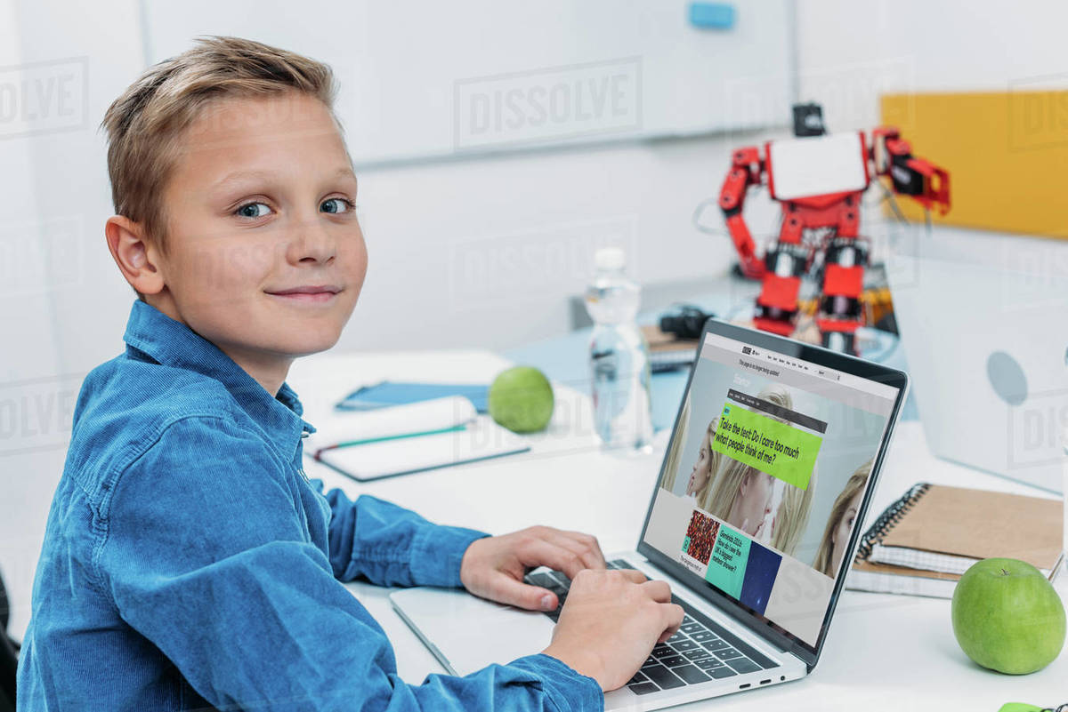 Smiling boy using laptop with science website on screen and taking ...