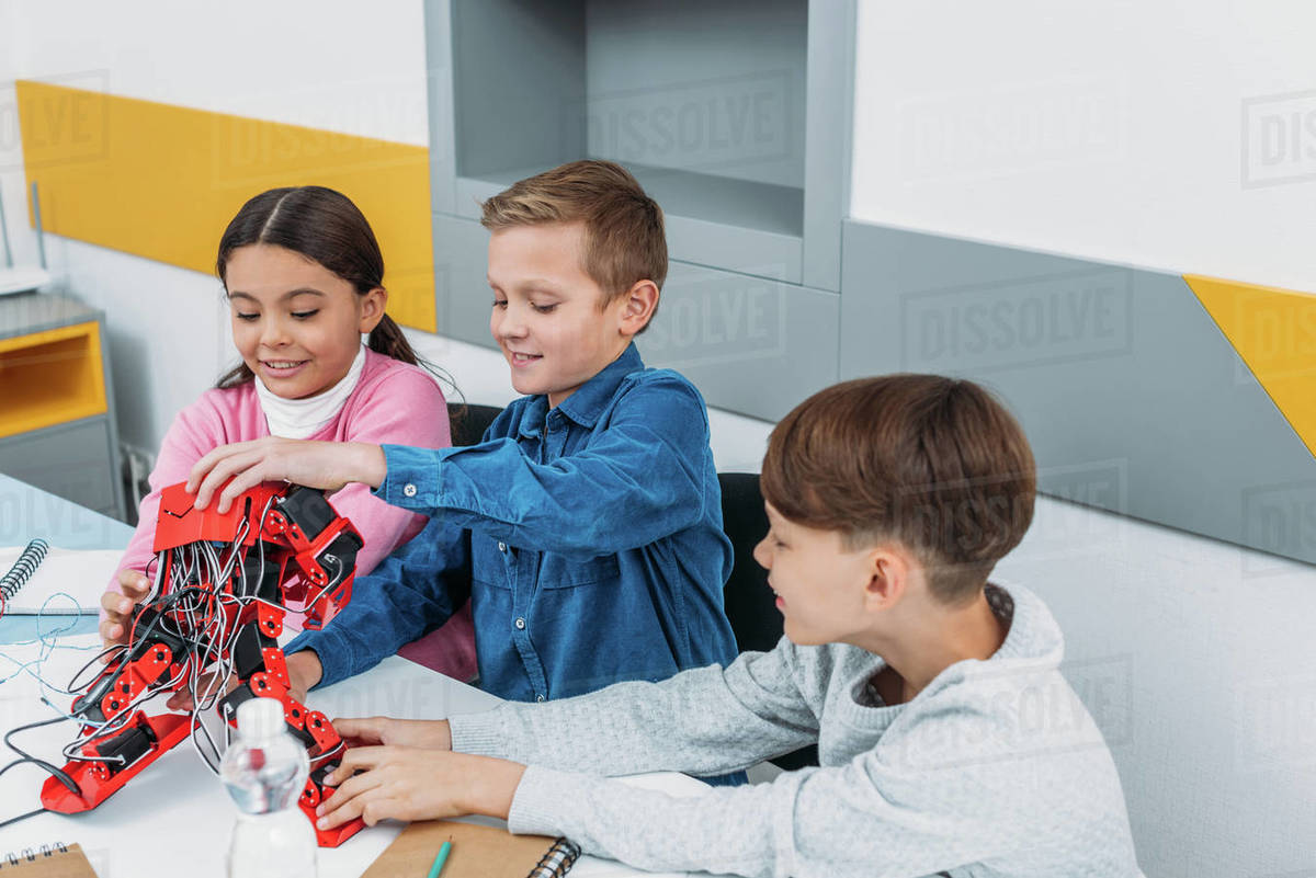 Smiling schoolchildren touching red electric robot on desk in stem ...