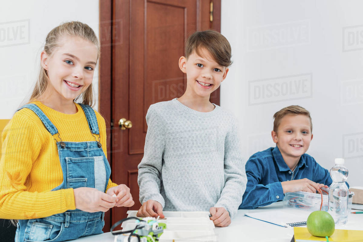 Happy classmates at desk looking at camera and working in stem ...