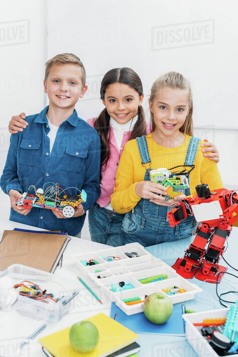 Smiling schoolchildren looking at camera and holding handmade robots in ...