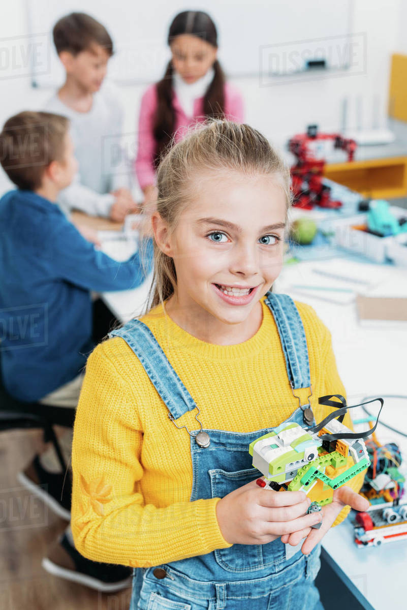 Preteen schoolgirl holding multicolored robot and looking at camera in ...