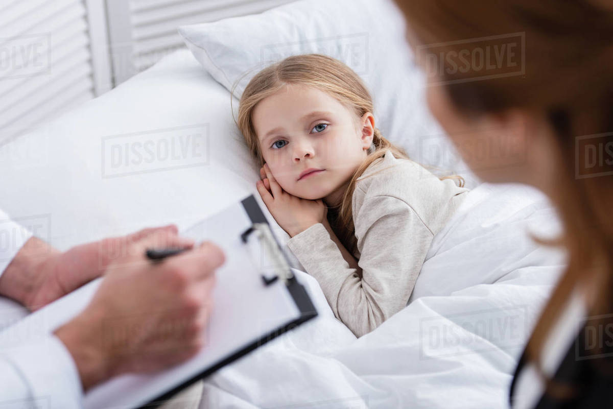 Selective focus of pediatrist writing something in clipboard, sick kid ...