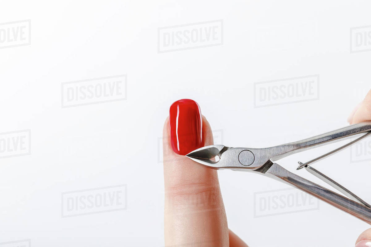 Manicurist using cuticle nipper on fingernail with red nail polish ...
