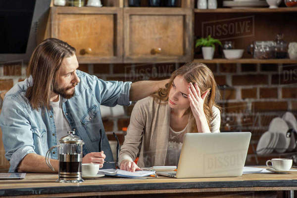 Young upset couple sitting with papers and laptop while working at home ...