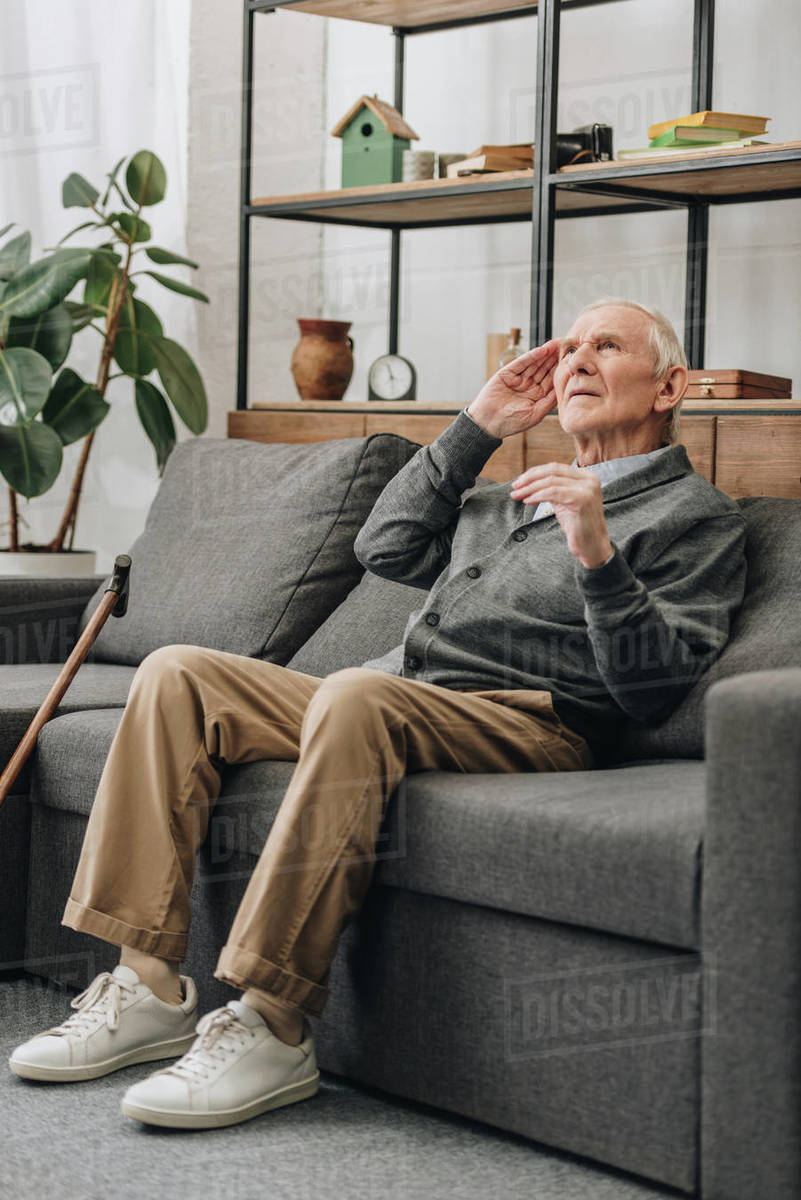 Dreamy senior man with grey hair sitting on sofa in living room ...